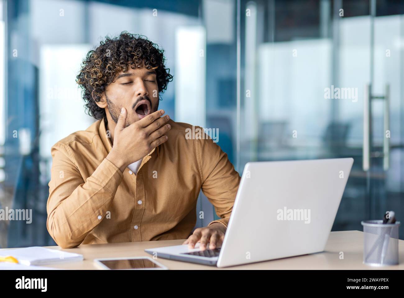 Young overworked and overtired businessman yawning, working inside ...