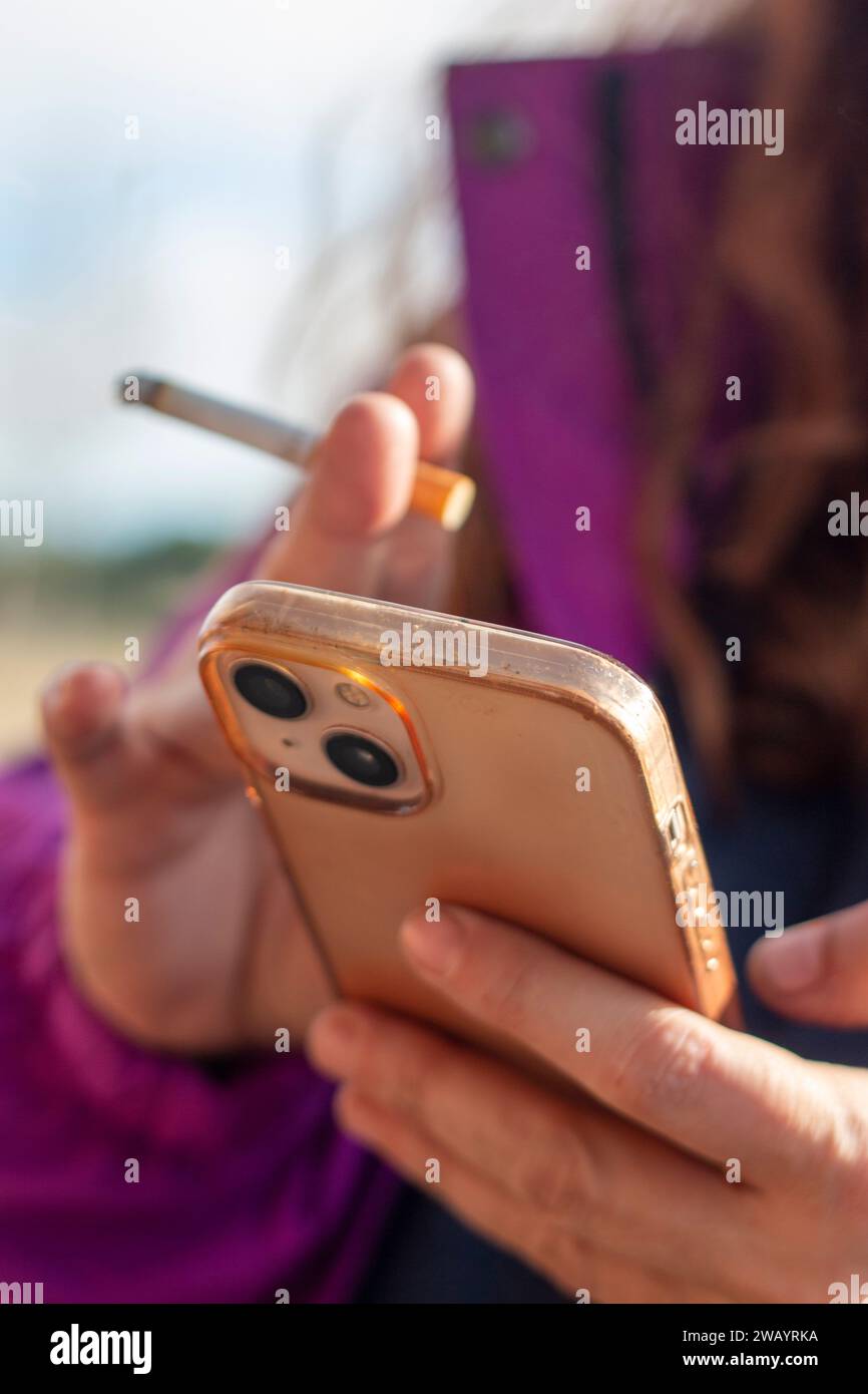 Woman's hand holding a smoking cigarette while using her mobile phone ...