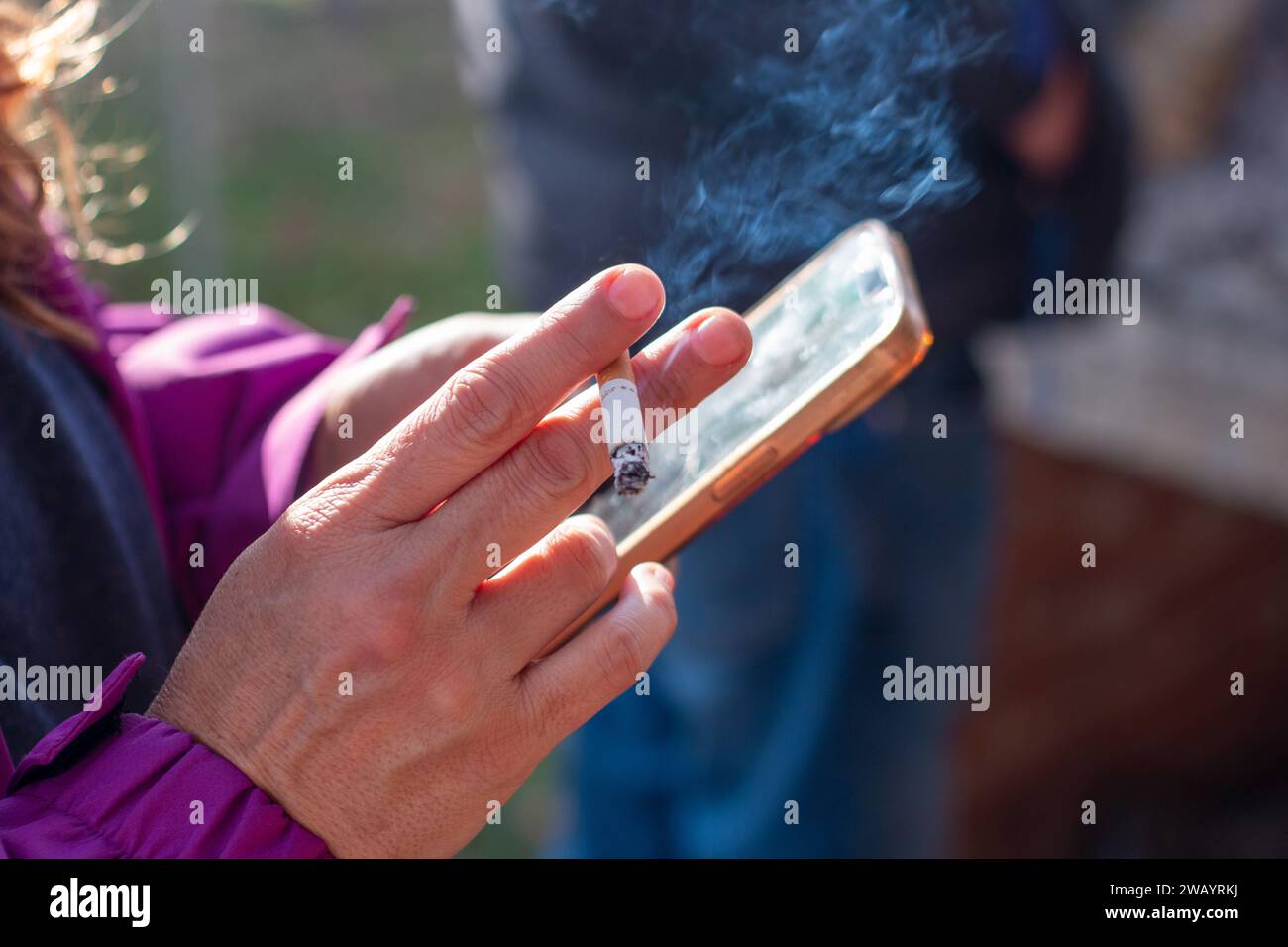 Woman's hand holding a smoking cigarette while using her mobile phone ...