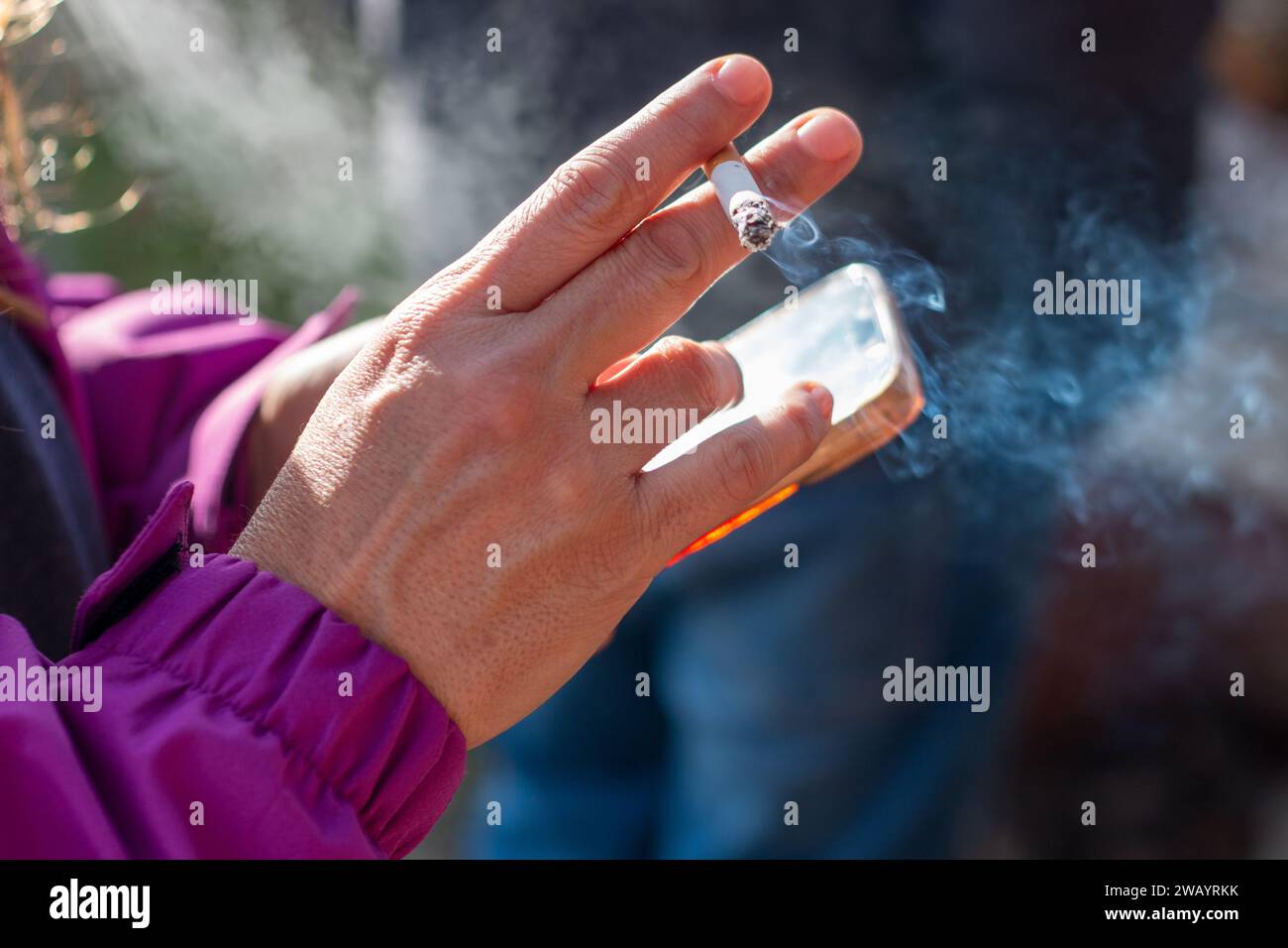 Woman's hand holding a smoking cigarette while using her mobile phone ...