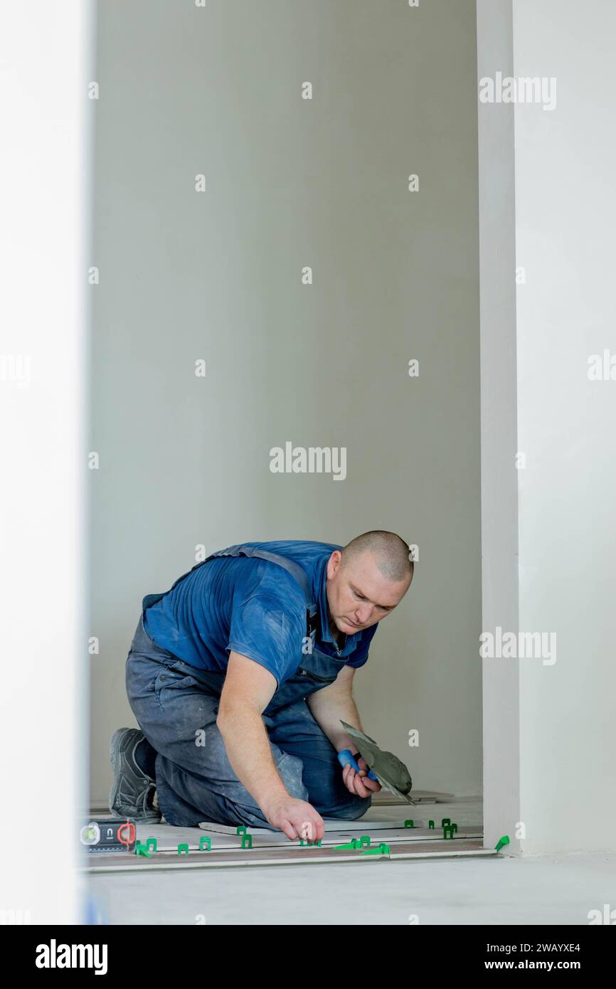 Tiler placing ceramic wall tile in position over adhesive with lash ...