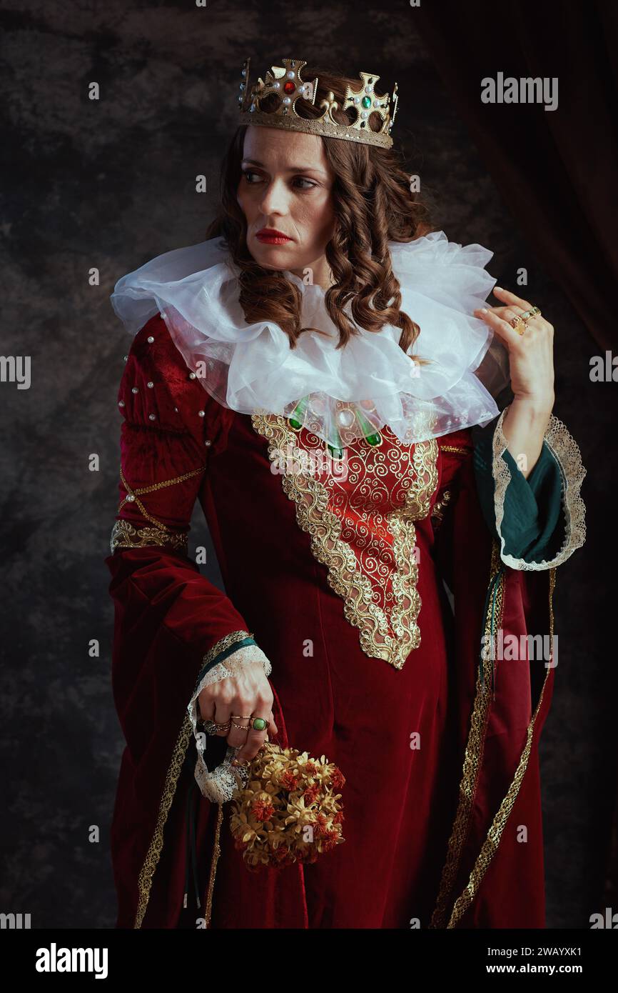 stressed medieval queen in red dress with dried flower, white collar ...