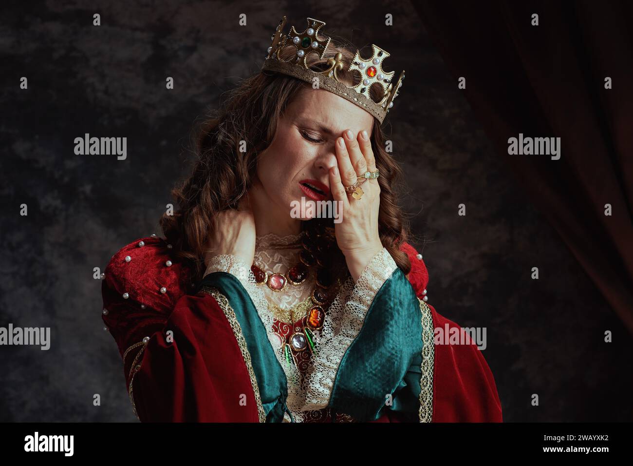 stressed medieval queen in red dress with crown having neck pain on ...