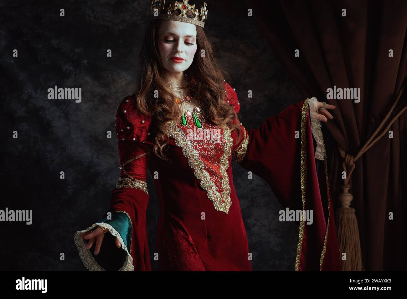 medieval queen in red dress with white makeup and crown on dark gray ...
