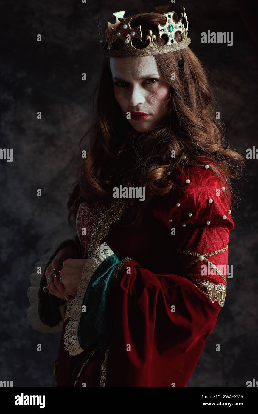 scary medieval queen in red dress with white makeup and crown on dark ...