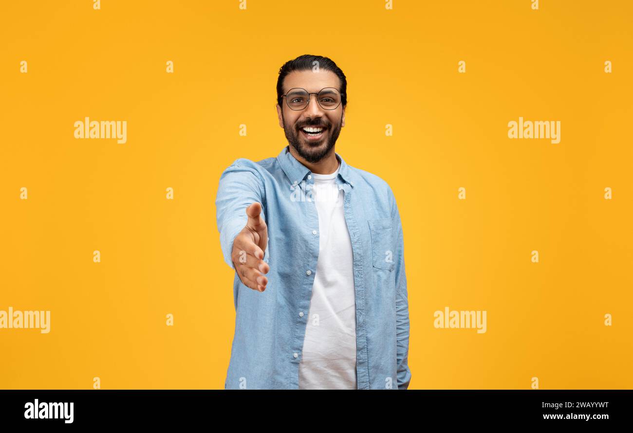 Amiable man in a denim shirt reaching out for a handshake, smiling ...