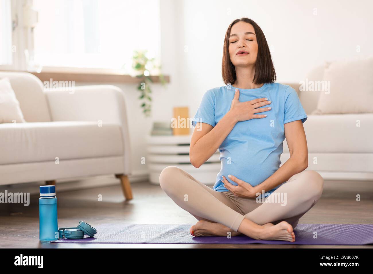 Expectant pregnant woman on yoga mat doing breathing exercises indoor ...