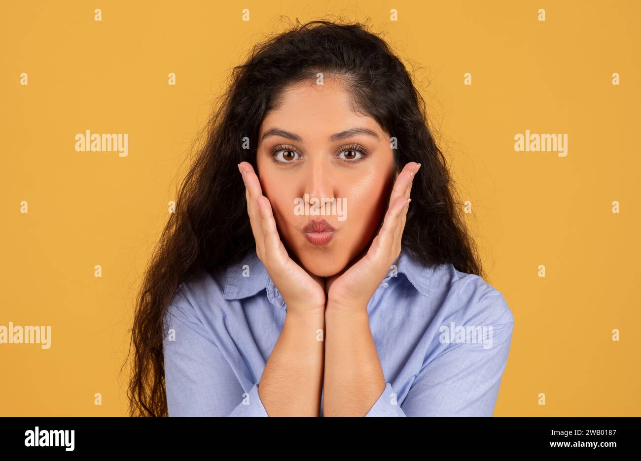 Surprised young woman with curly hair making a playful pout, hands on ...