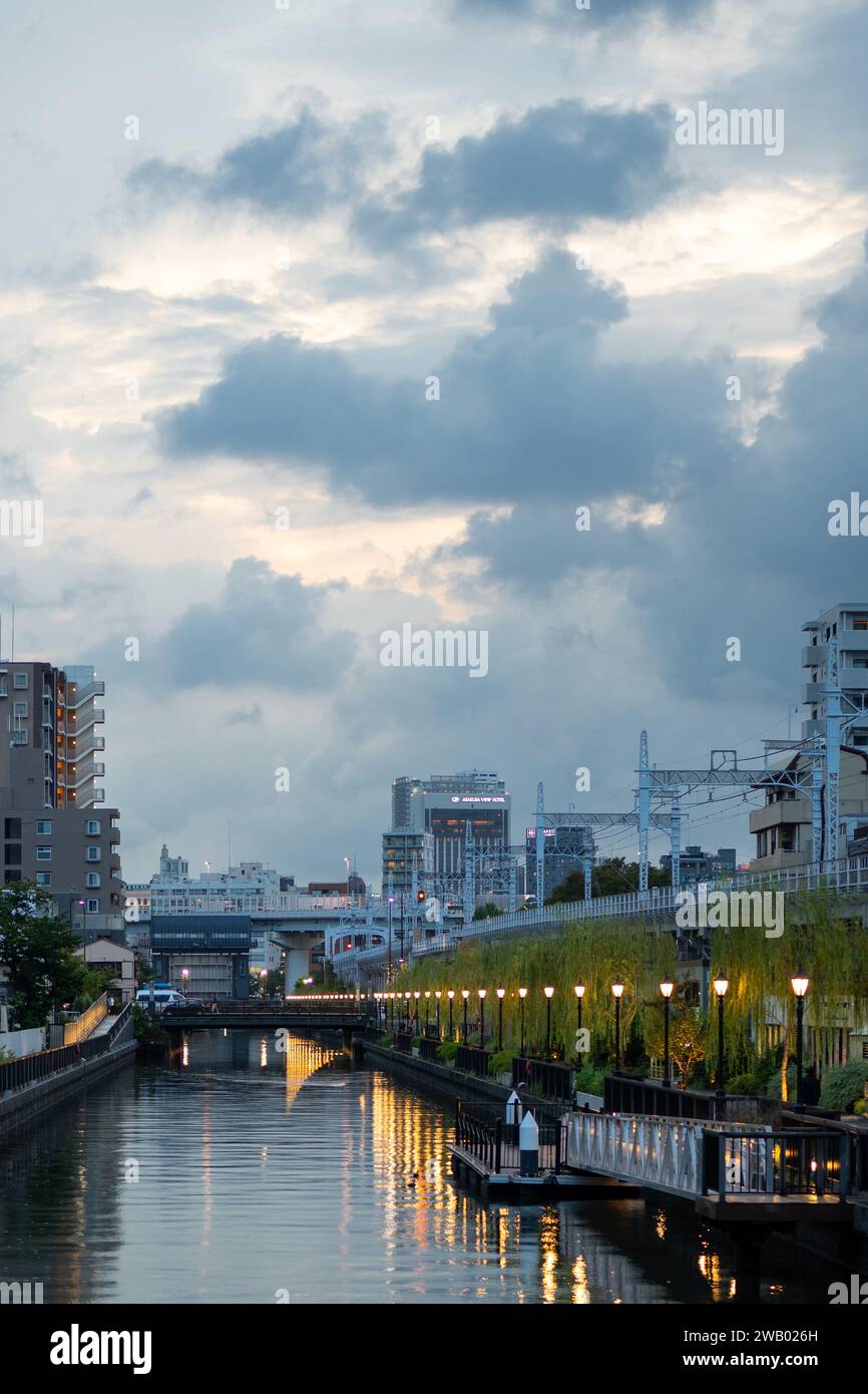 cloudy sunset over a canal in central tokyo along an elevated train ...