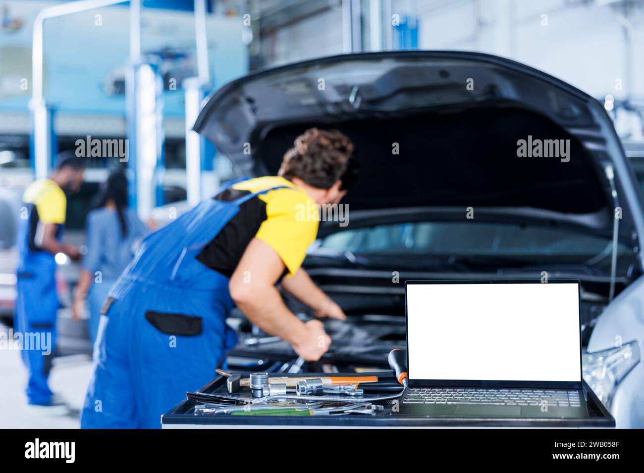 Mockup laptop on car service work station bench with technician in ...