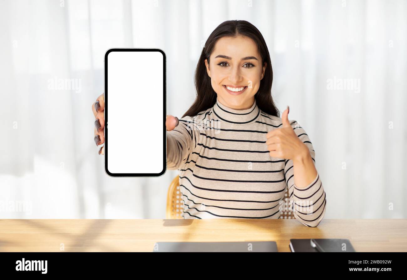 Millennial smiling arab lady show phone with blank screen, show thumb ...
