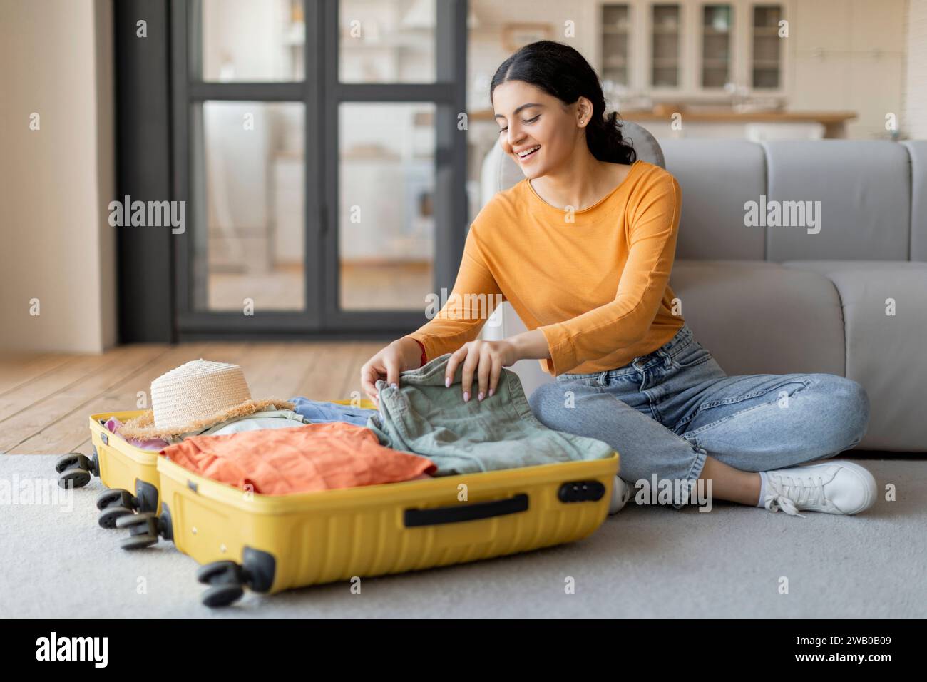 Smiling young indian woman happily packing suitcase at home Stock Photo ...