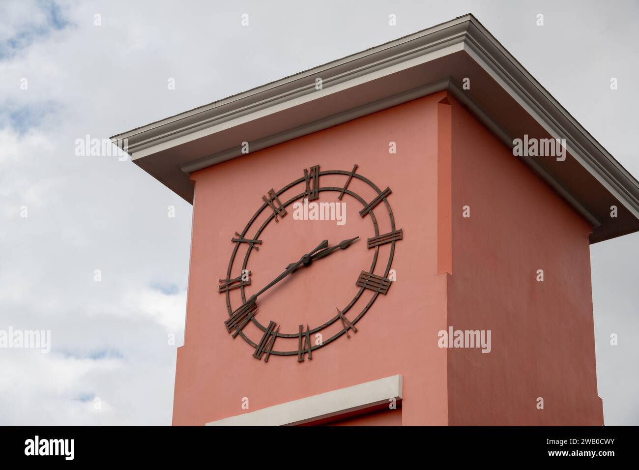 An exterior analog clock on a rose colored tower building with a cream ...