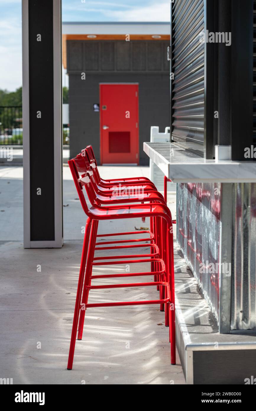 Three vibrant red metal bar chairs are in front of a stylish metal ...