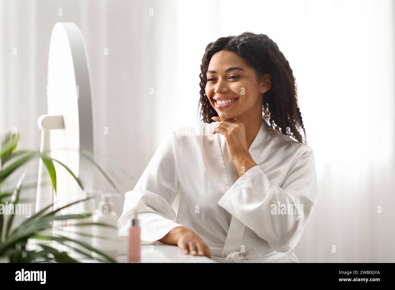 Beautiful black woman sitting at dressing table at home and touching ...