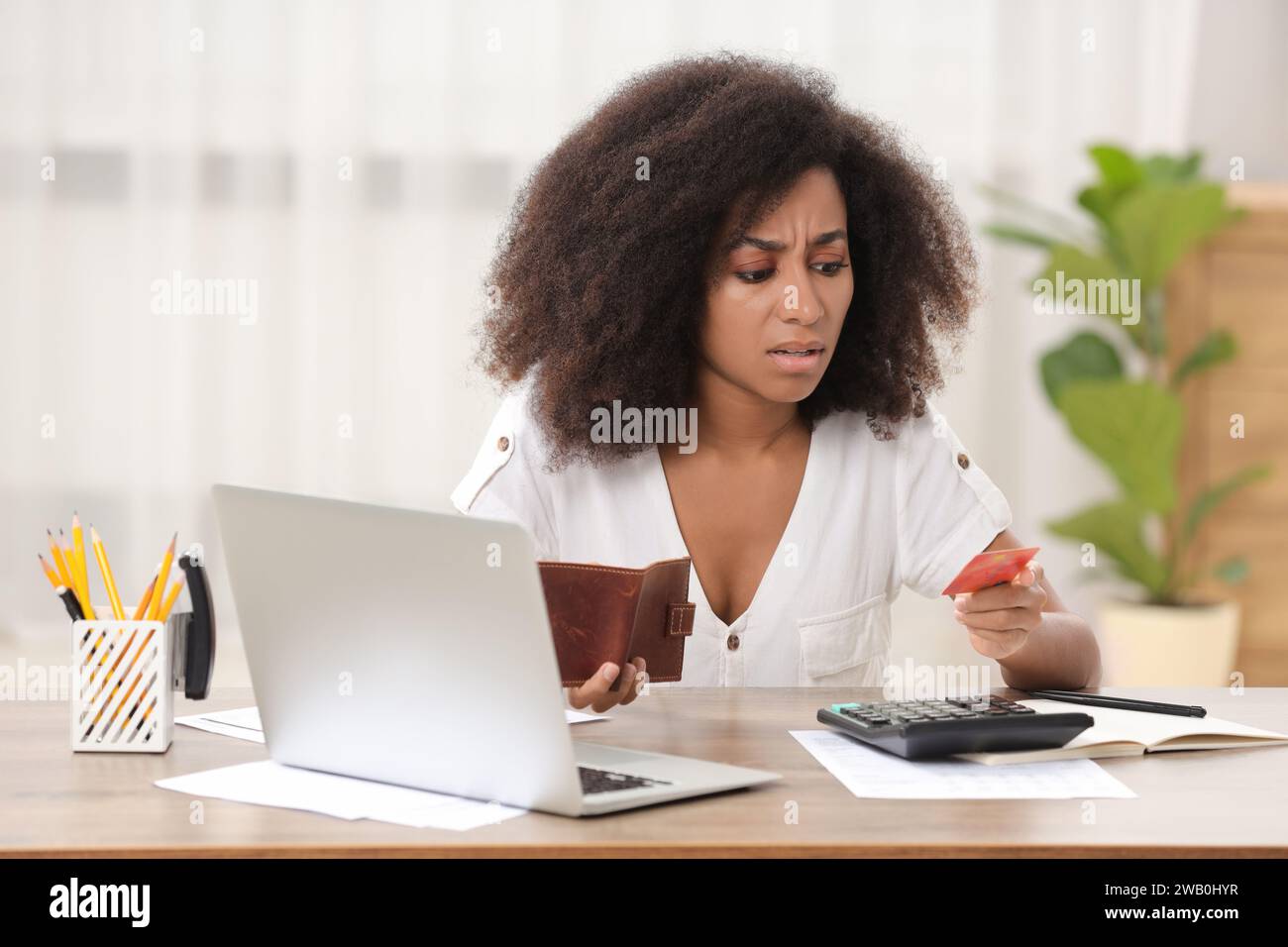Confused woman with credit card and wallet planning budget at table in ...
