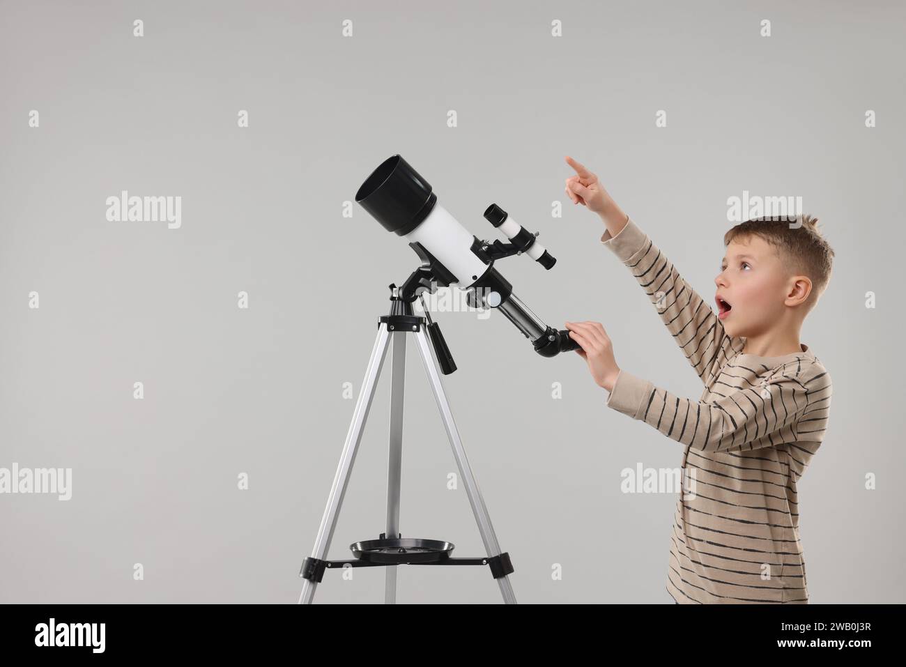 Surprised little boy with telescope pointing at something on light grey ...