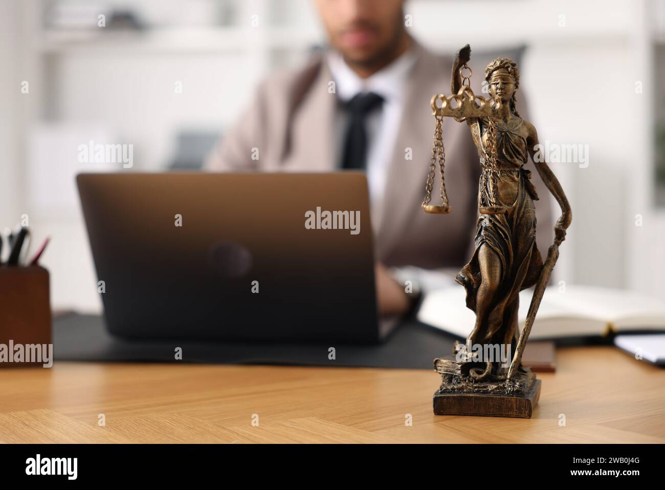 Lawyer working with laptop at table in office, focus on statue of Lady ...