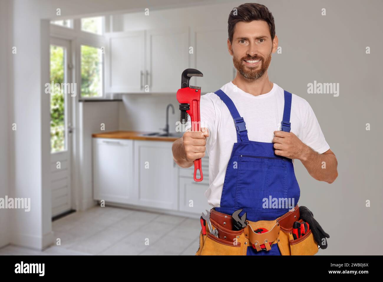 Plumber with pipe wrench and tool belt in kitchen, space for text Stock ...