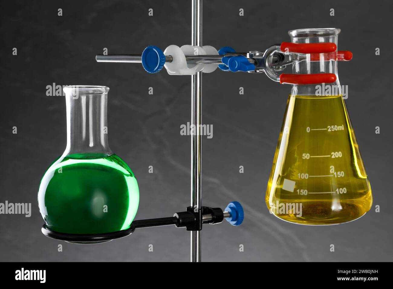 Retort stand and laboratory flasks with liquids on grey background ...