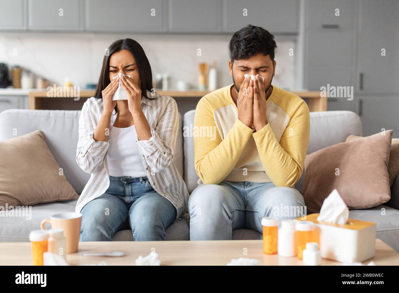 Sick indian couple sitting on sofa, blowing noses and suffering from ...