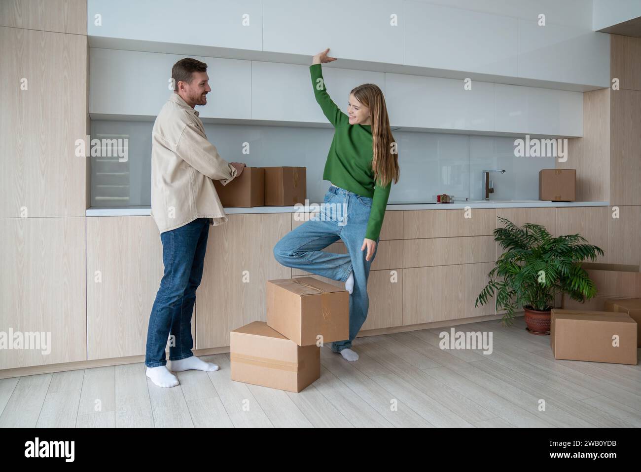 Happy tired young family couple talking on kitchen among boxes moving ...