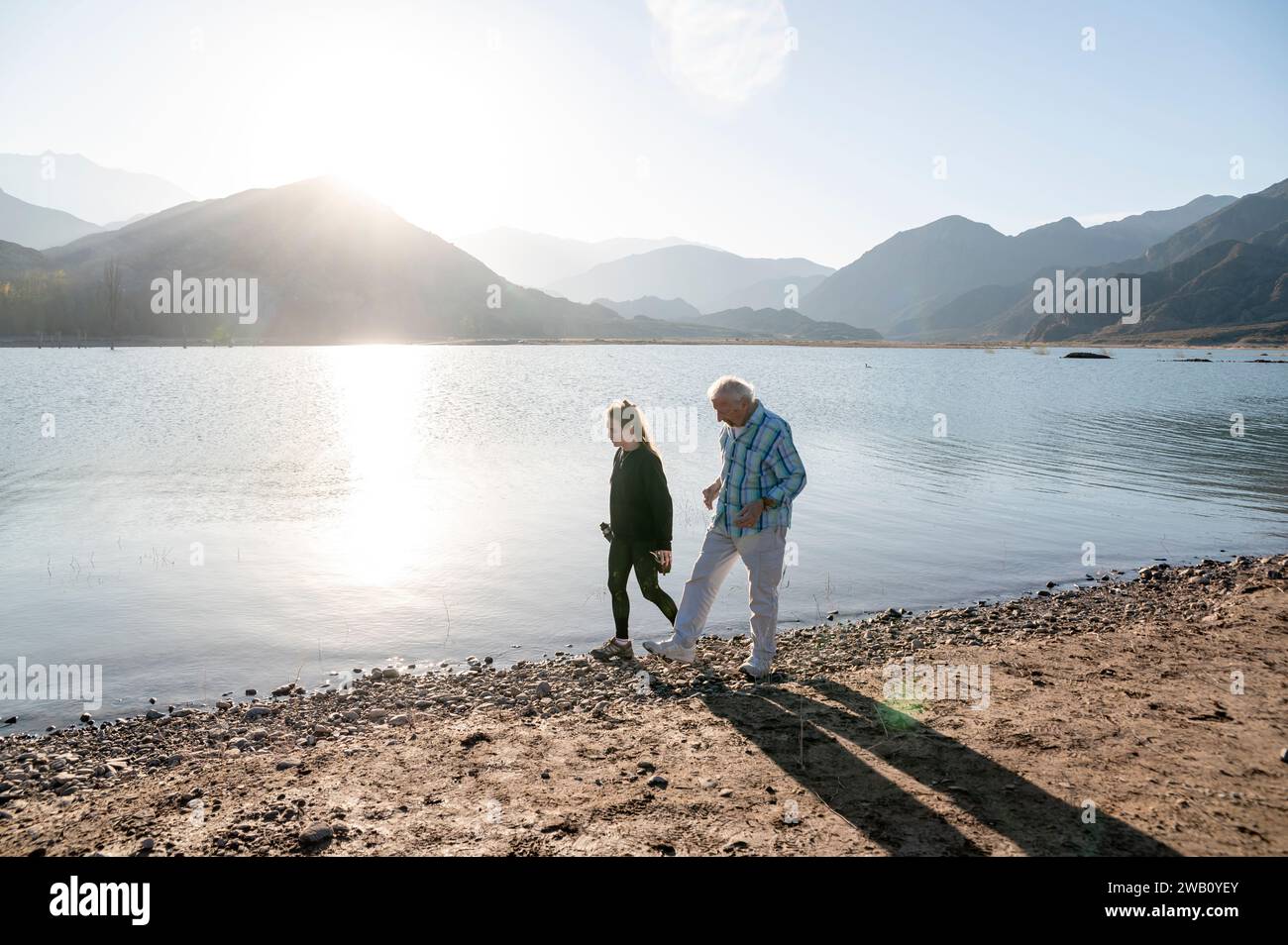 Senior man walking with his granddaughter along the lake shore with ...