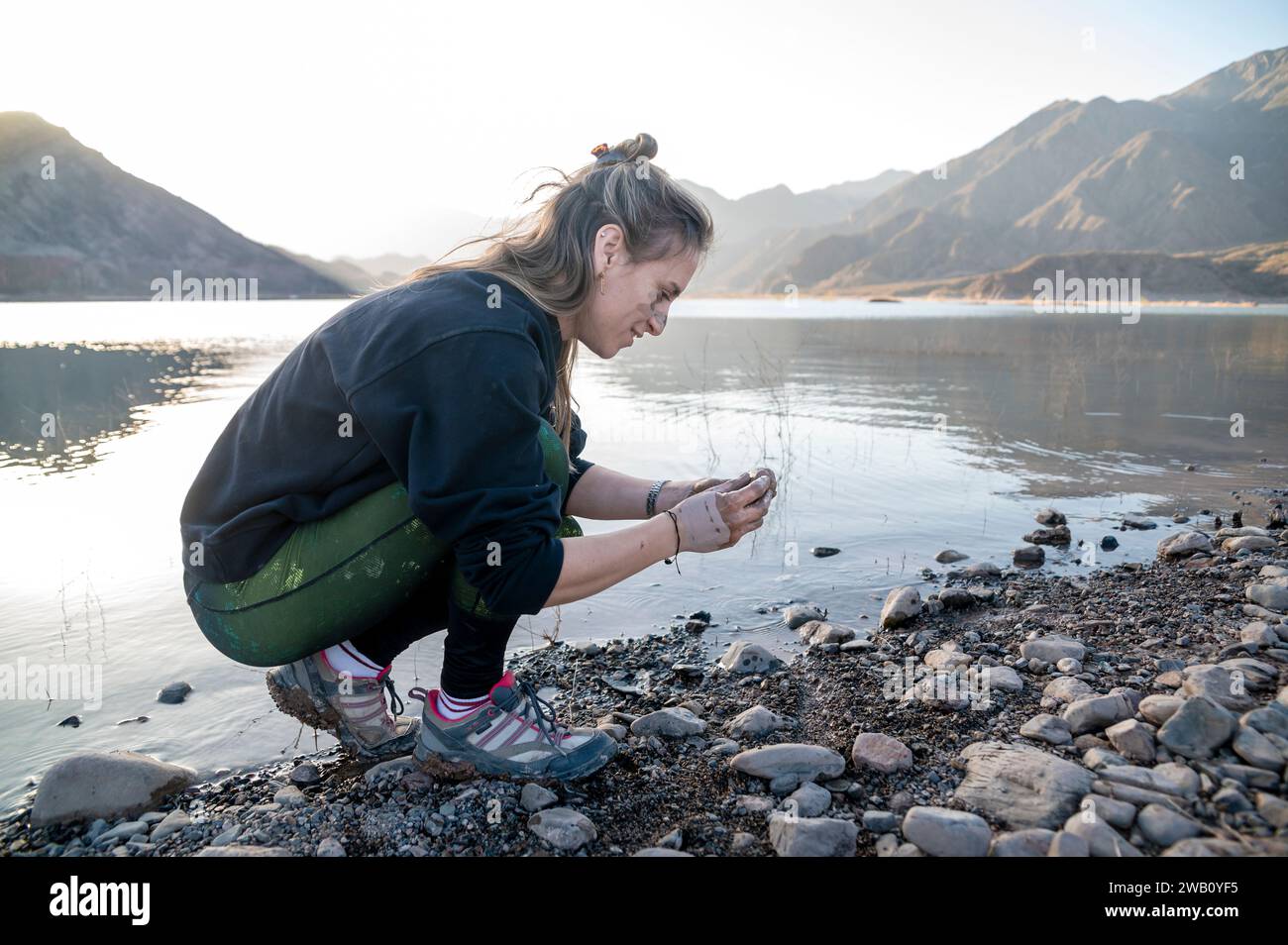 Woman putting mud on hands and face while enjoying outdoors in nature ...