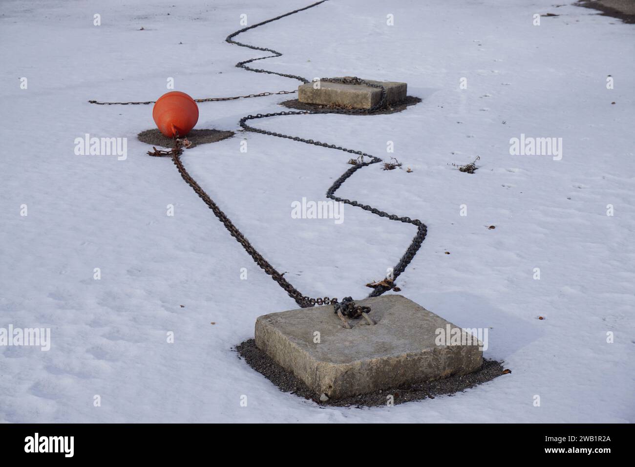 snow on a red buoy and cement weights for boats on shore with a curvy ...