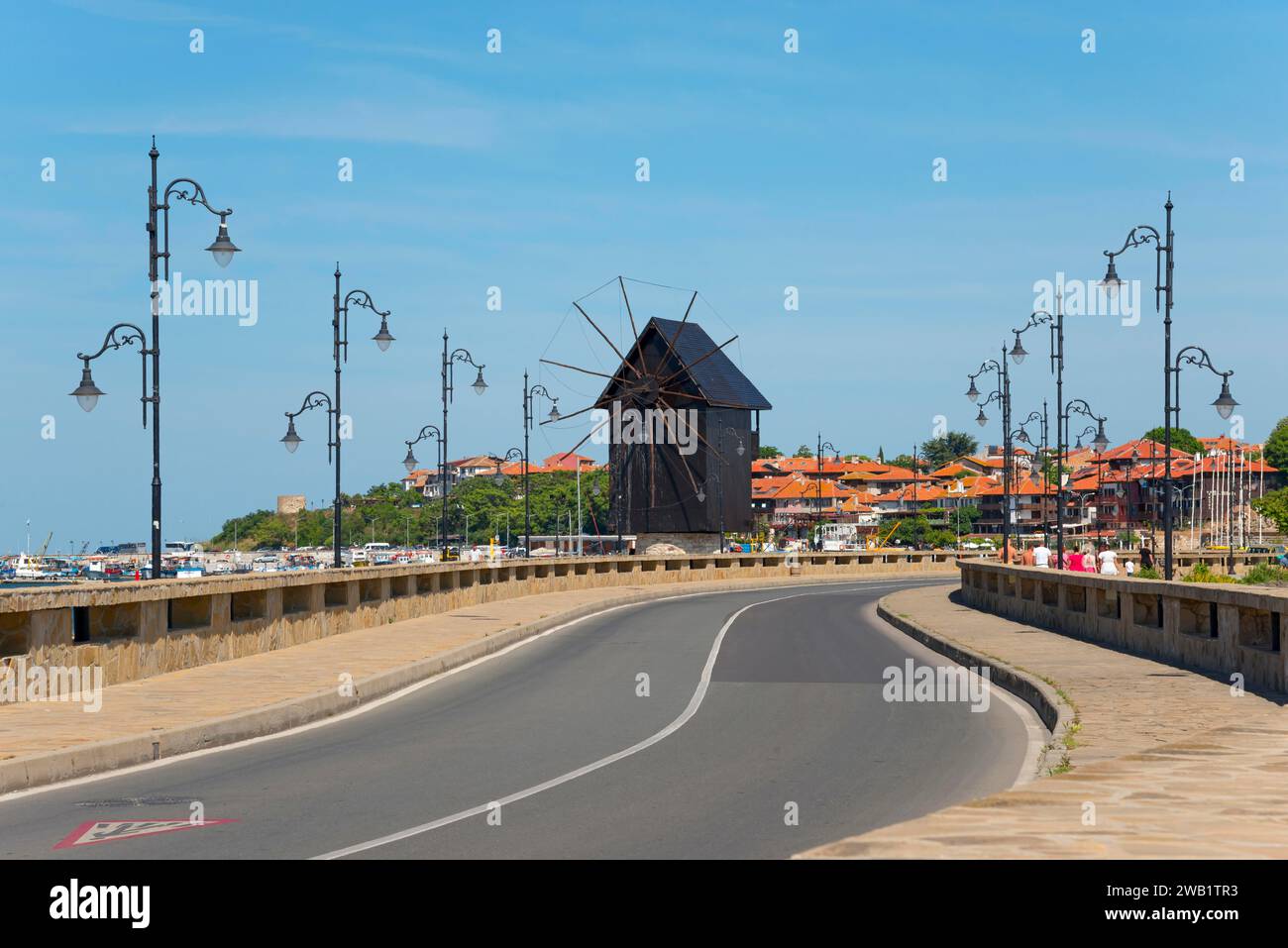 A tidy coastal road leads to a traditional windmill under a bright blue ...