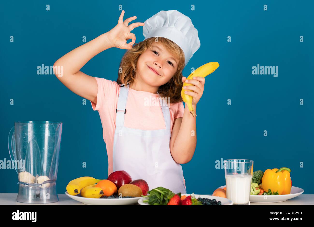 Child chef cook prepares food hold banana in isolated blue studio ...
