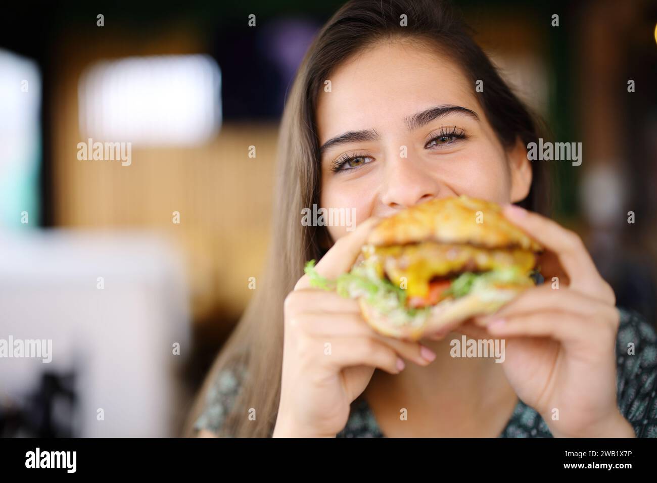 Happy woman eating burger looking at you in a restaurant Stock Photo ...