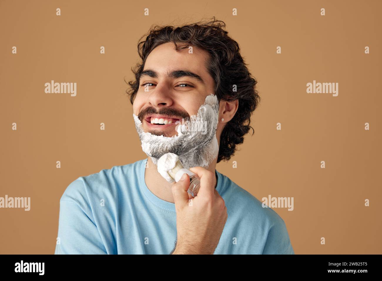 Portrait of young positive brunette man with curly hair applies shaving ...