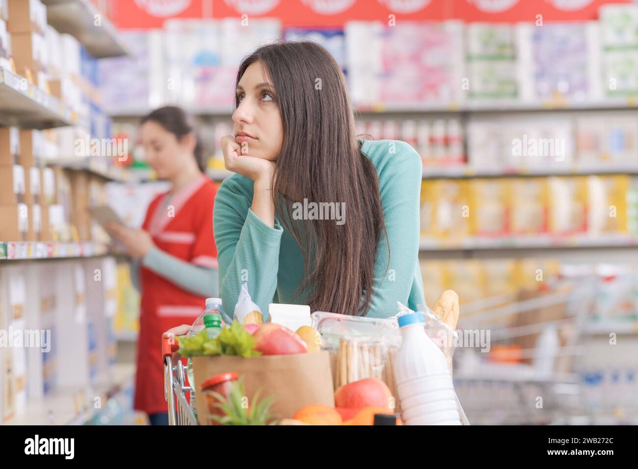 Bored young woman leaning on the shopping cart at the grocery store ...