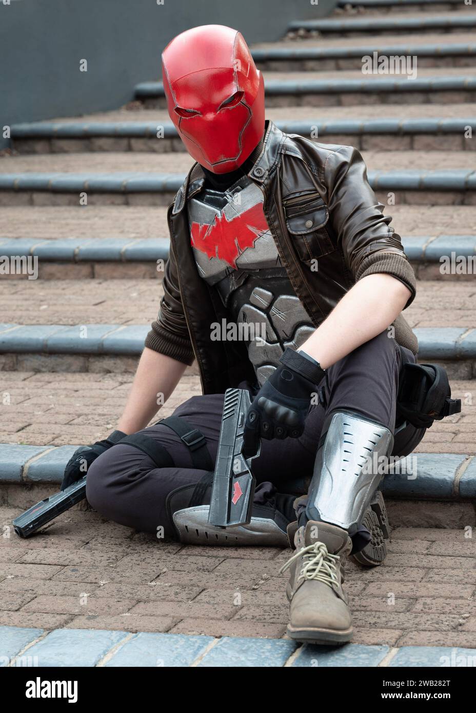 A male cosplayer in a costume with a red helmet, leather jacket, and ...