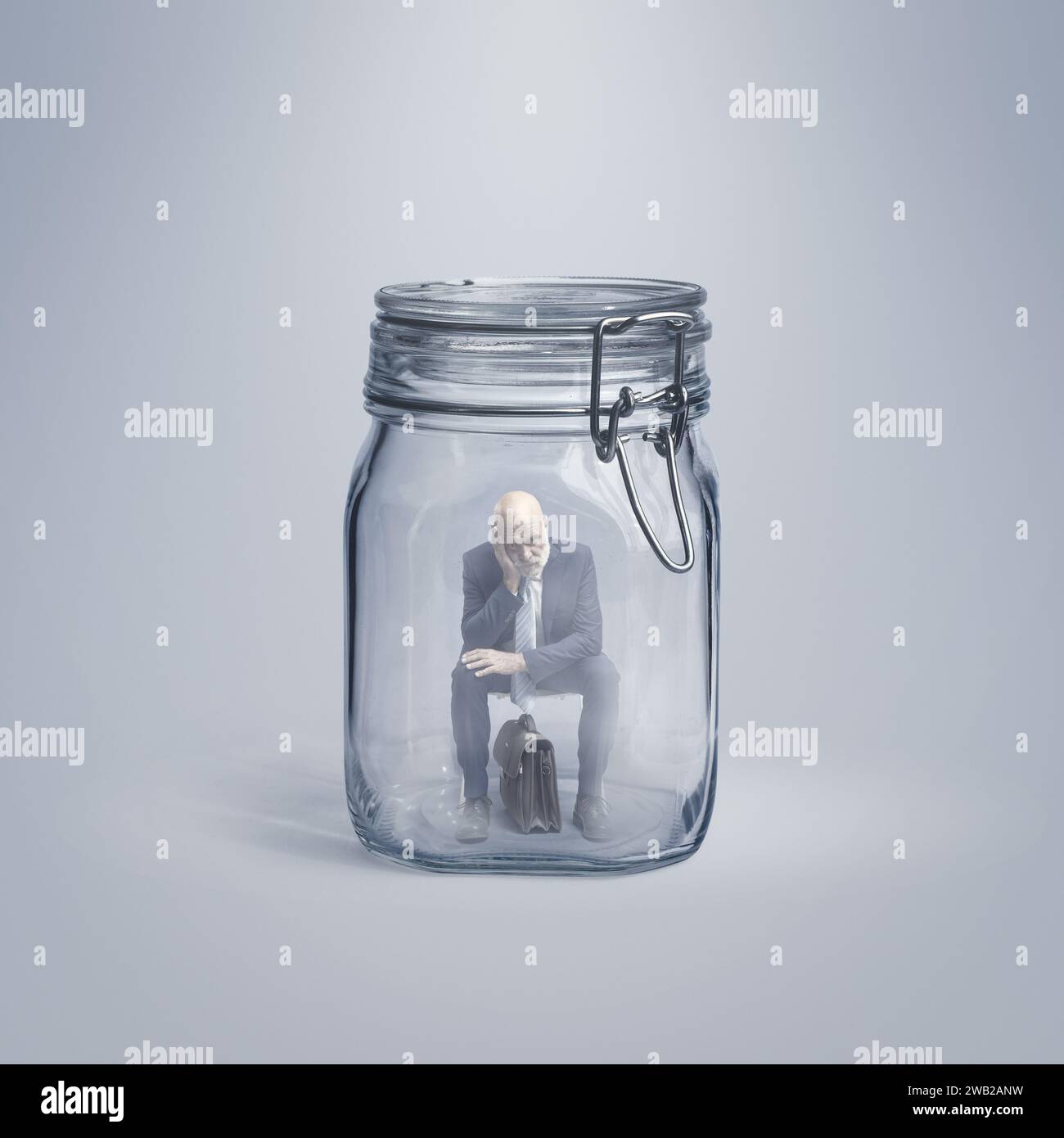 Hopeless senior businessman trapped inside a glass jar, he is sitting ...