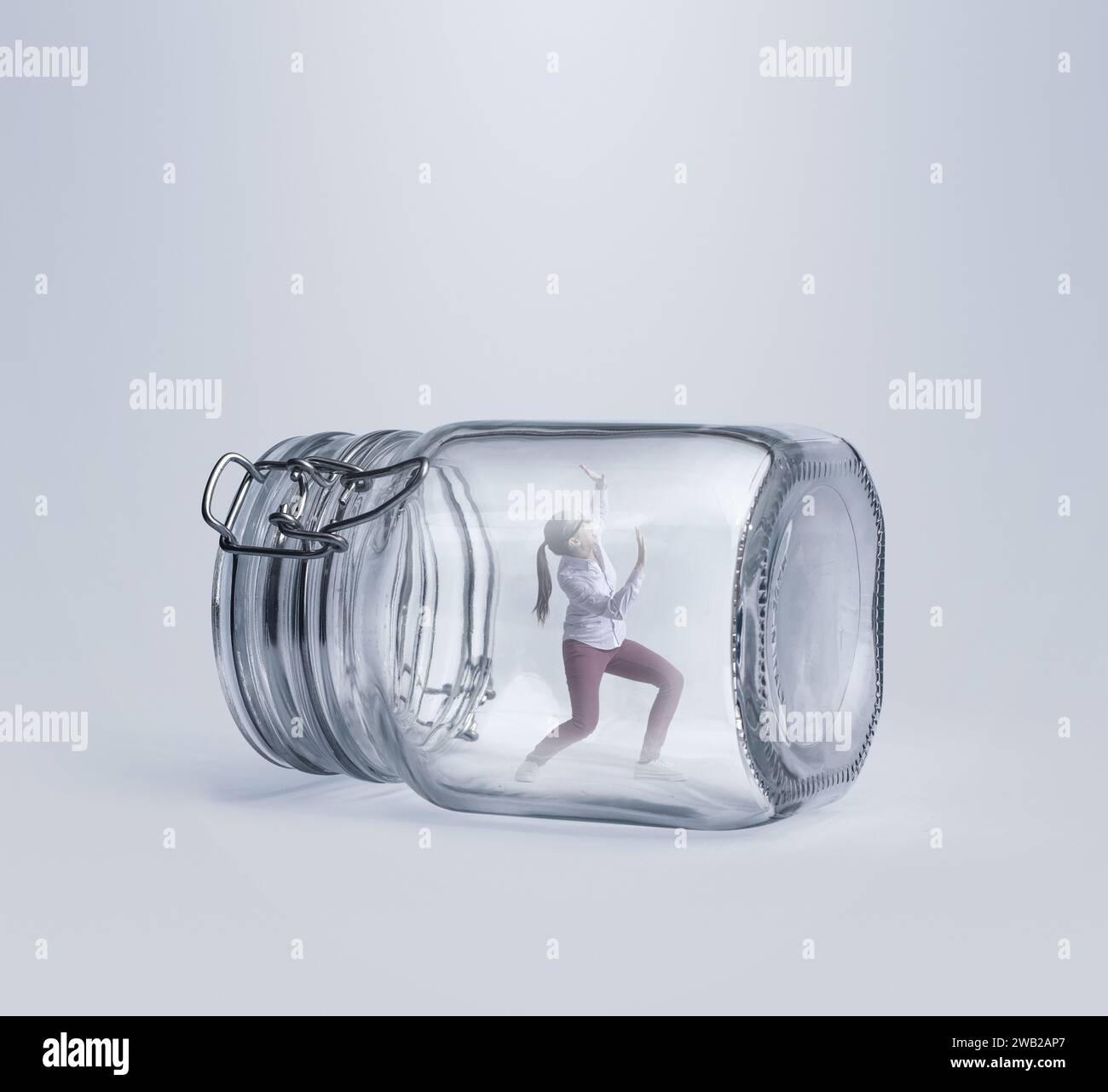 Scared young woman trapped in a huge glass jar, she is desperate and unable to escape Stock ...