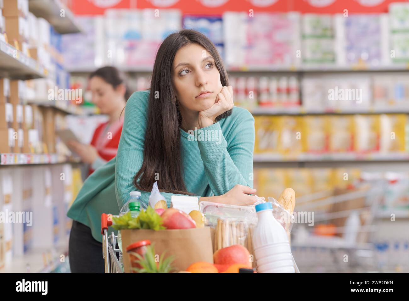 Bored young woman leaning on the shopping cart at the grocery store ...