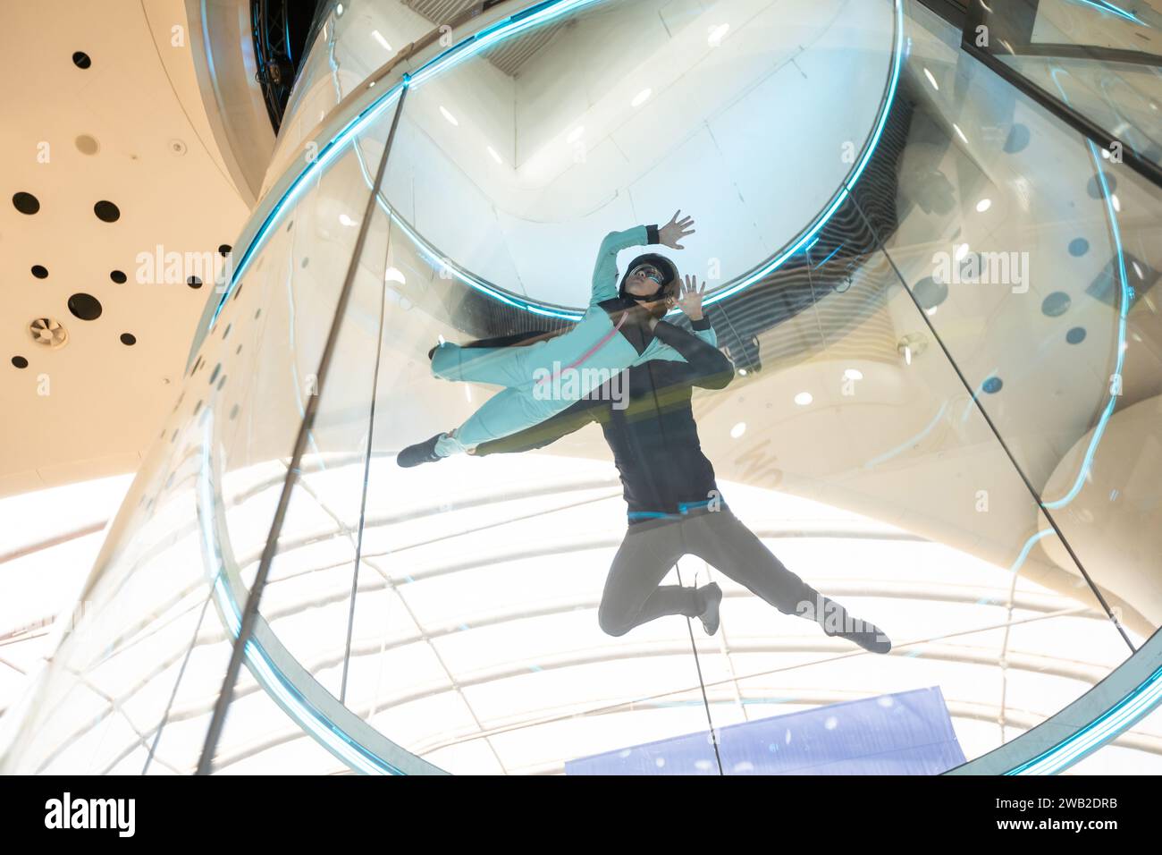 Excited teenage girl in helmet flying in aerodynamic tube wind tunnel ...