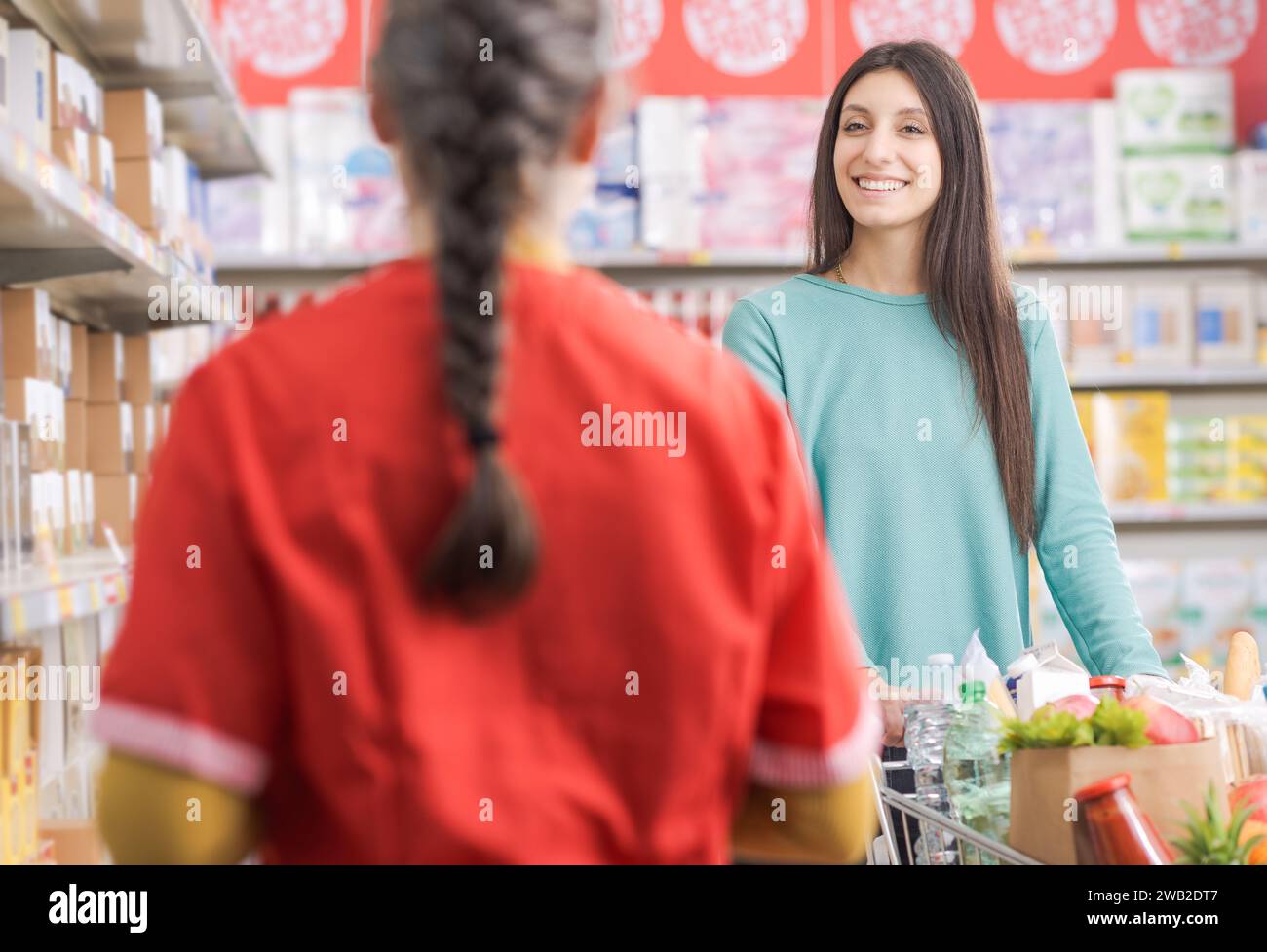 Smiling woman buying groceries at the supermarket, she is pushing a ...