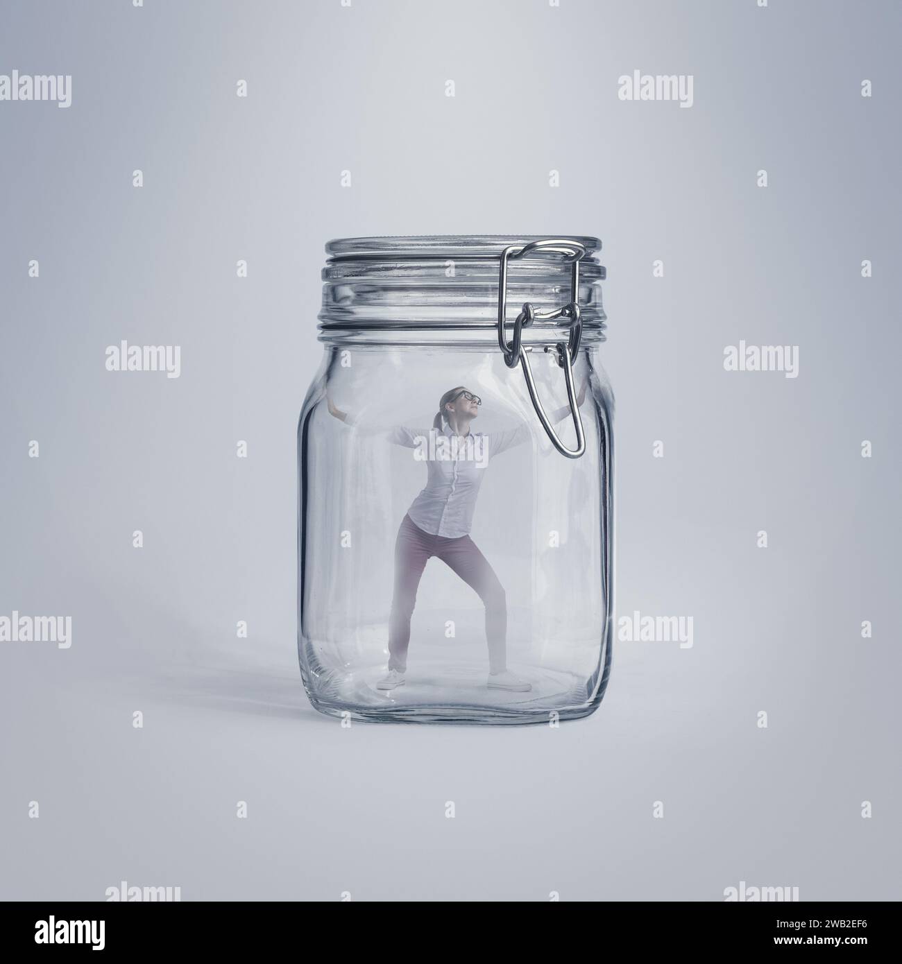 Scared young woman trapped in a huge glass jar, she is desperate and ...