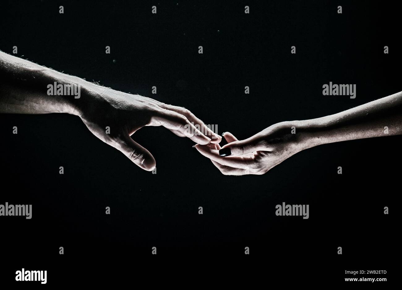 Two hands stretch each other, black background. Couple in love holding ...
