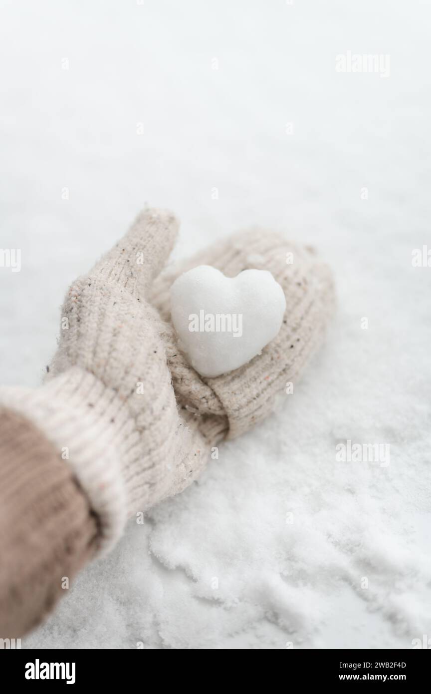 Hand in beige mitten holding heart shaped snowball on white background ...