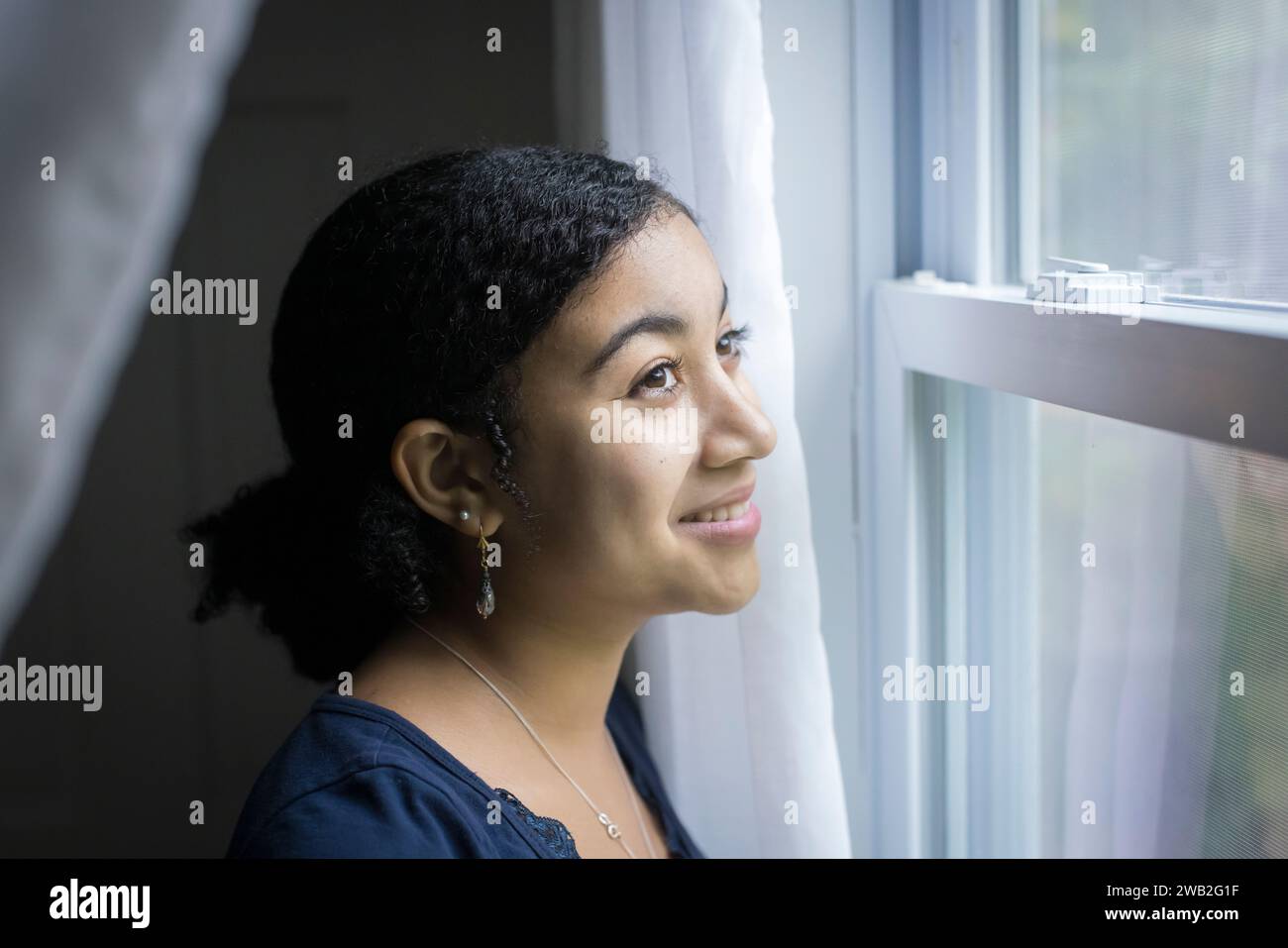 biracial teen girl looks out a window with a smile on her face Stock ...