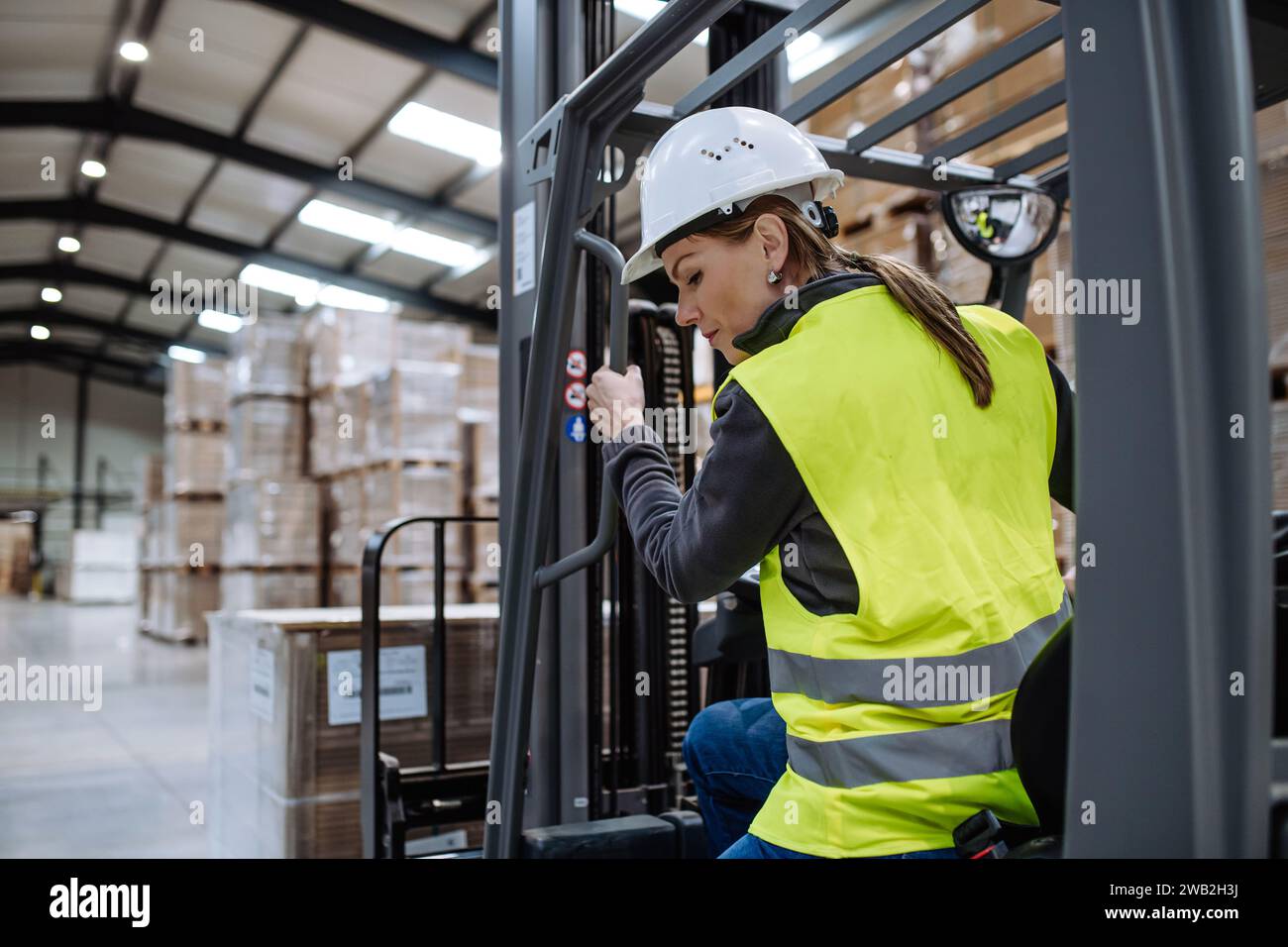 Female warehouse worker driving forklift. Warehouse worker preparing products for shipmennt ...