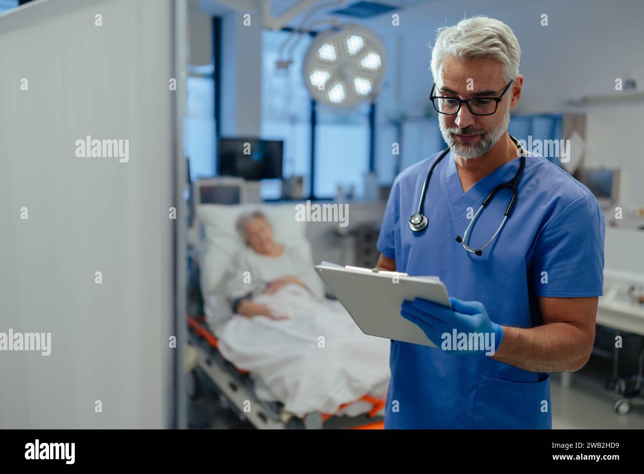 Portrait of handsome male doctor, patient in hospital bed behind. ER ...
