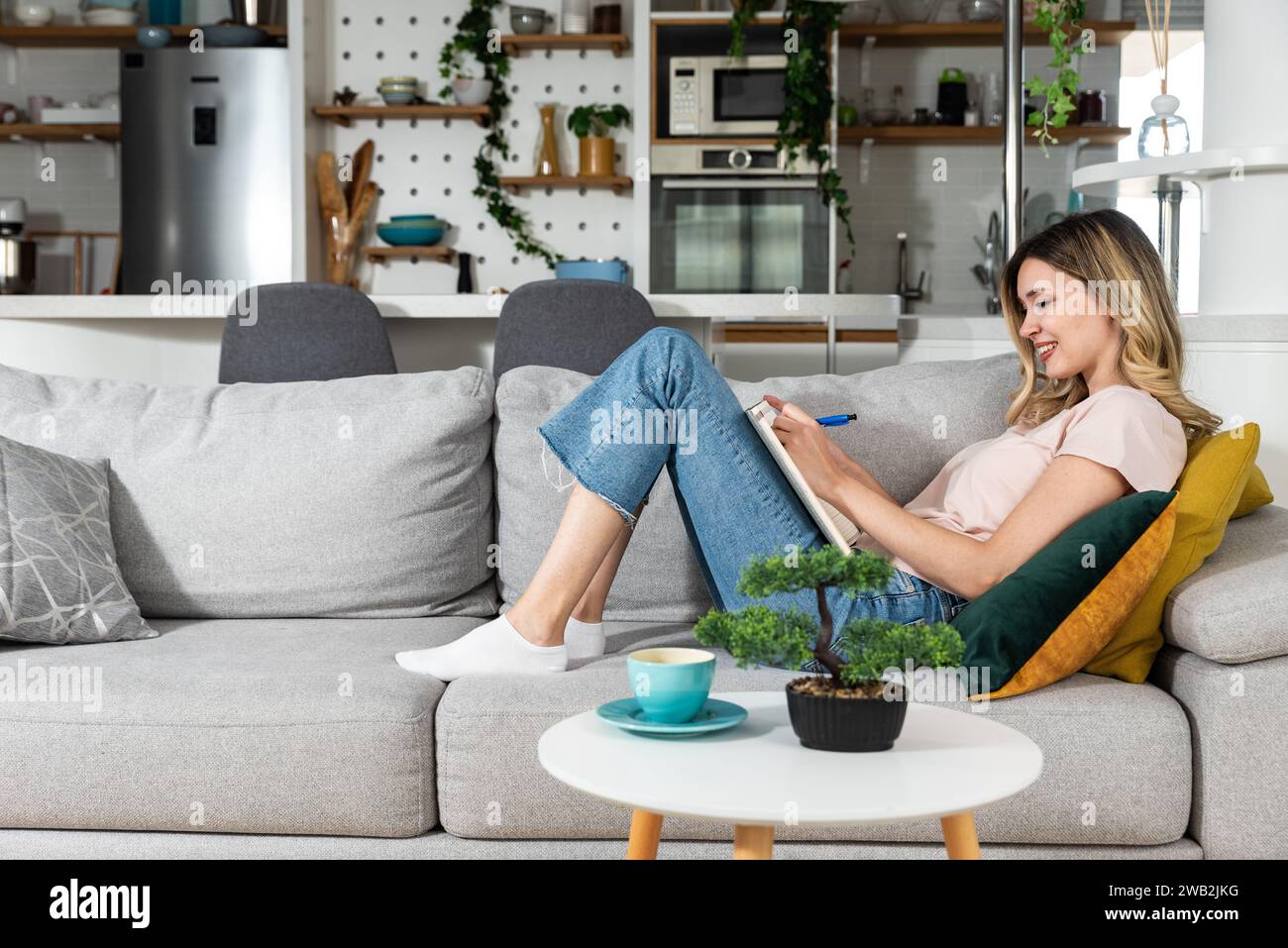 Young woman sitting on the sofa writing down the guest list of her ...