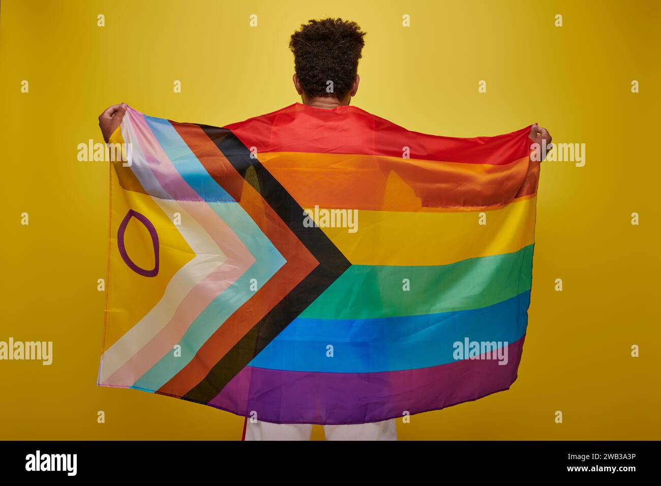 back view of african american man holding lgbtq rainbow flag on yellow ...