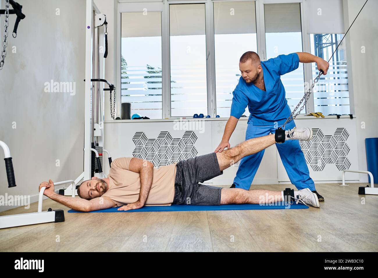 skilled rehabilitologist in blue uniform assisting man during recovery ...