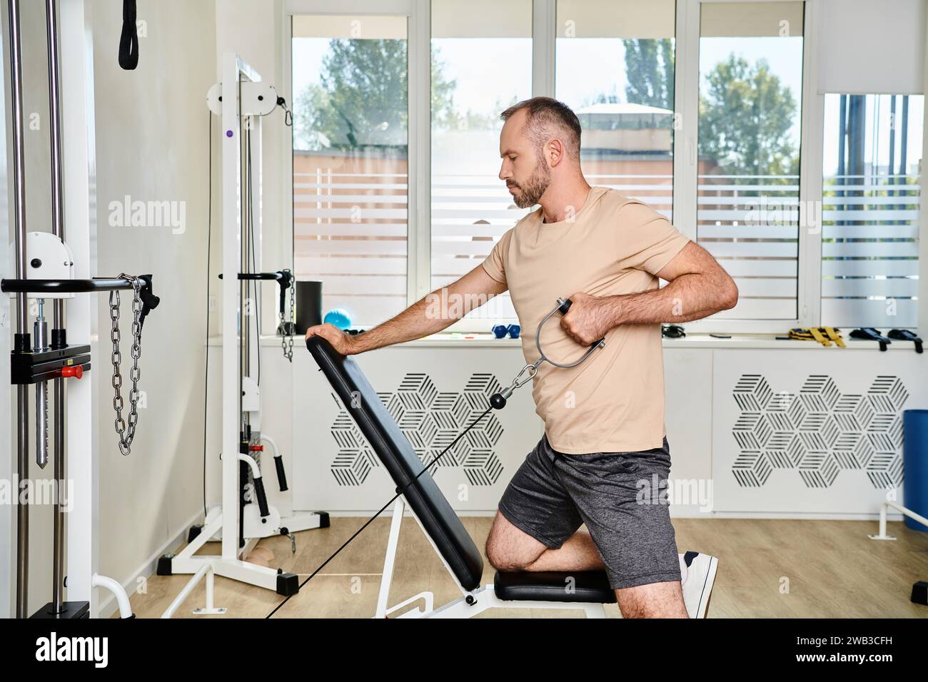 side view of bearded man in sportswear working out on exercise machine ...